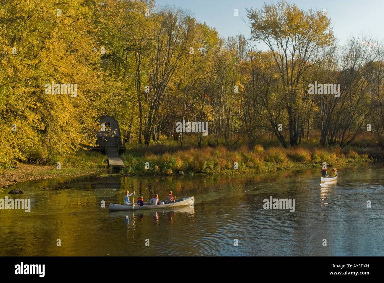 Kids and adults in two canoes paddling up the Concord River in autumn ...