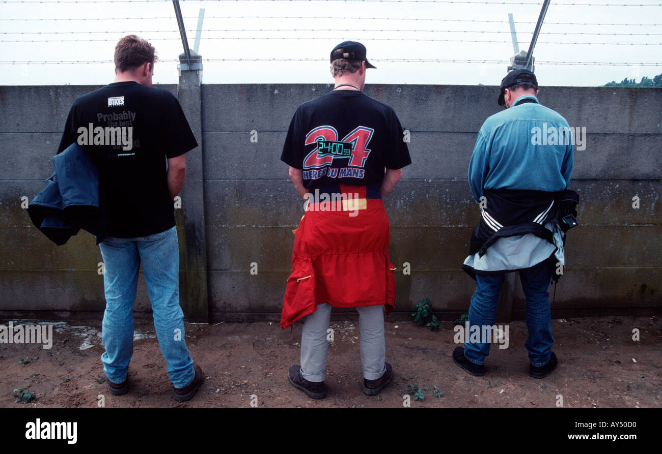 Back view of three blokes relieving themselves against a wall Stock ...