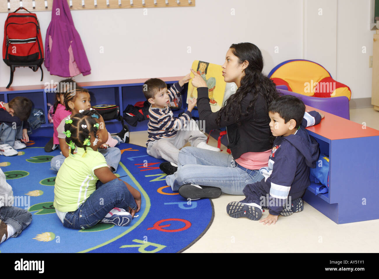 Preschool teacher reading a book to her class while the children sit on ...