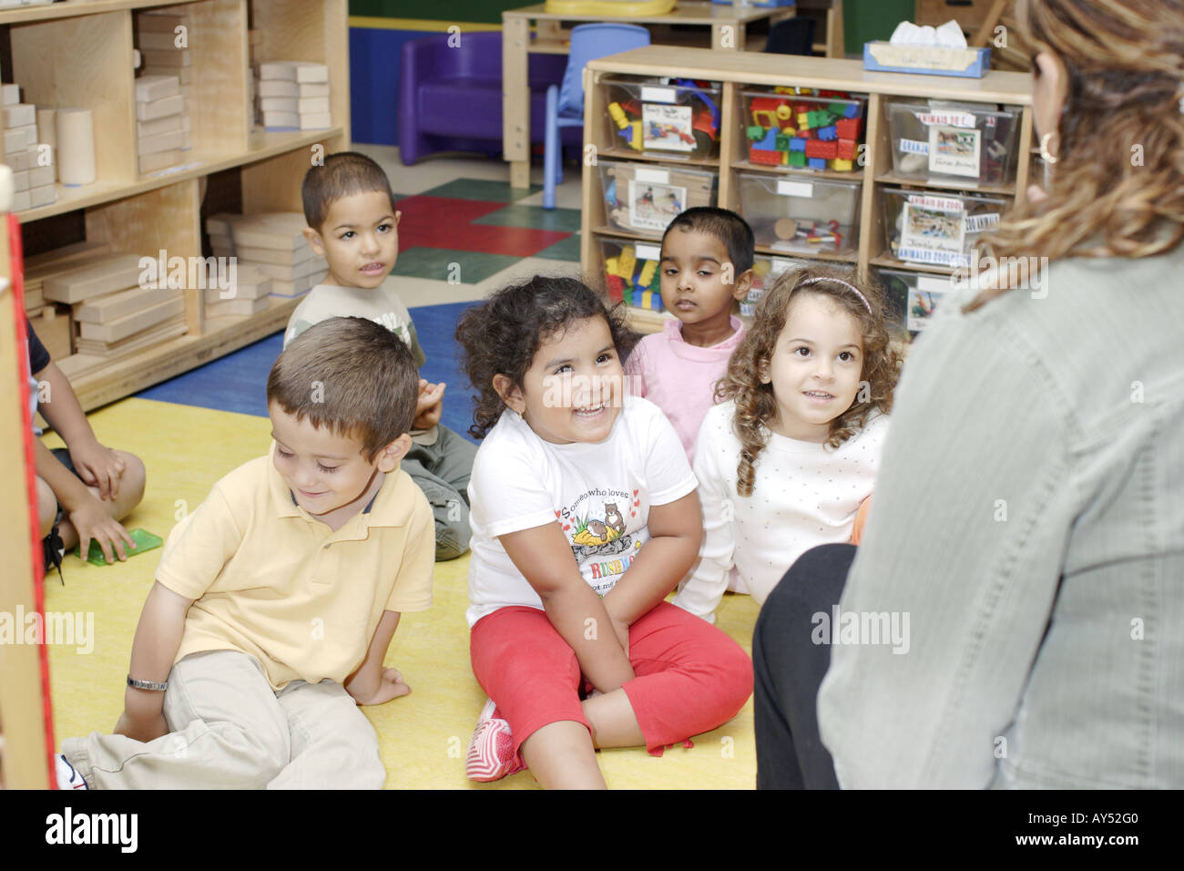 Preschool teacher talking to her class while the children sit on the ...