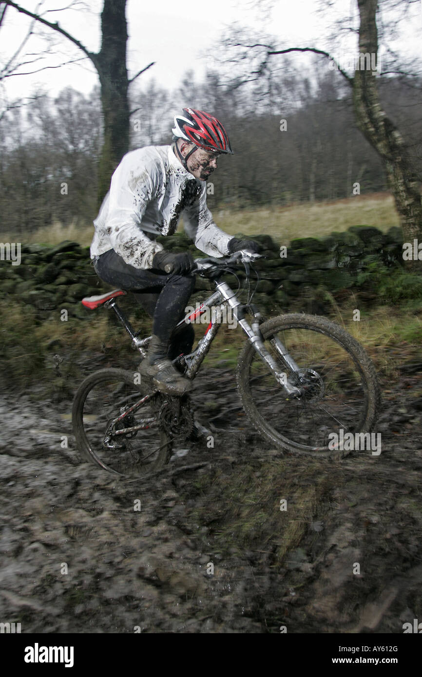 A mountain biker covered in mud rides his bike along a muddy track ...
