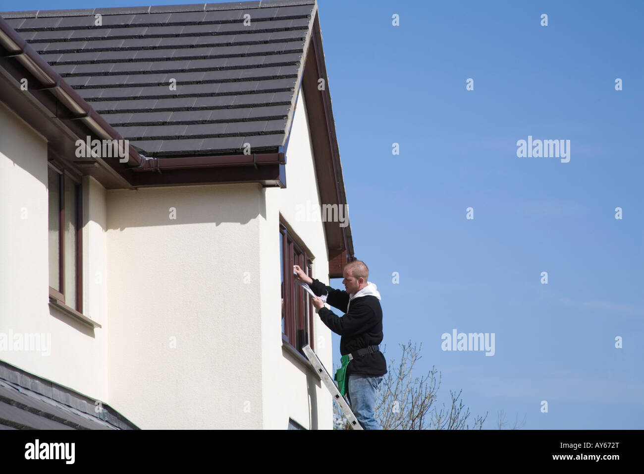 North Wales UK March A young male window cleaner cleaning the bedroom ...