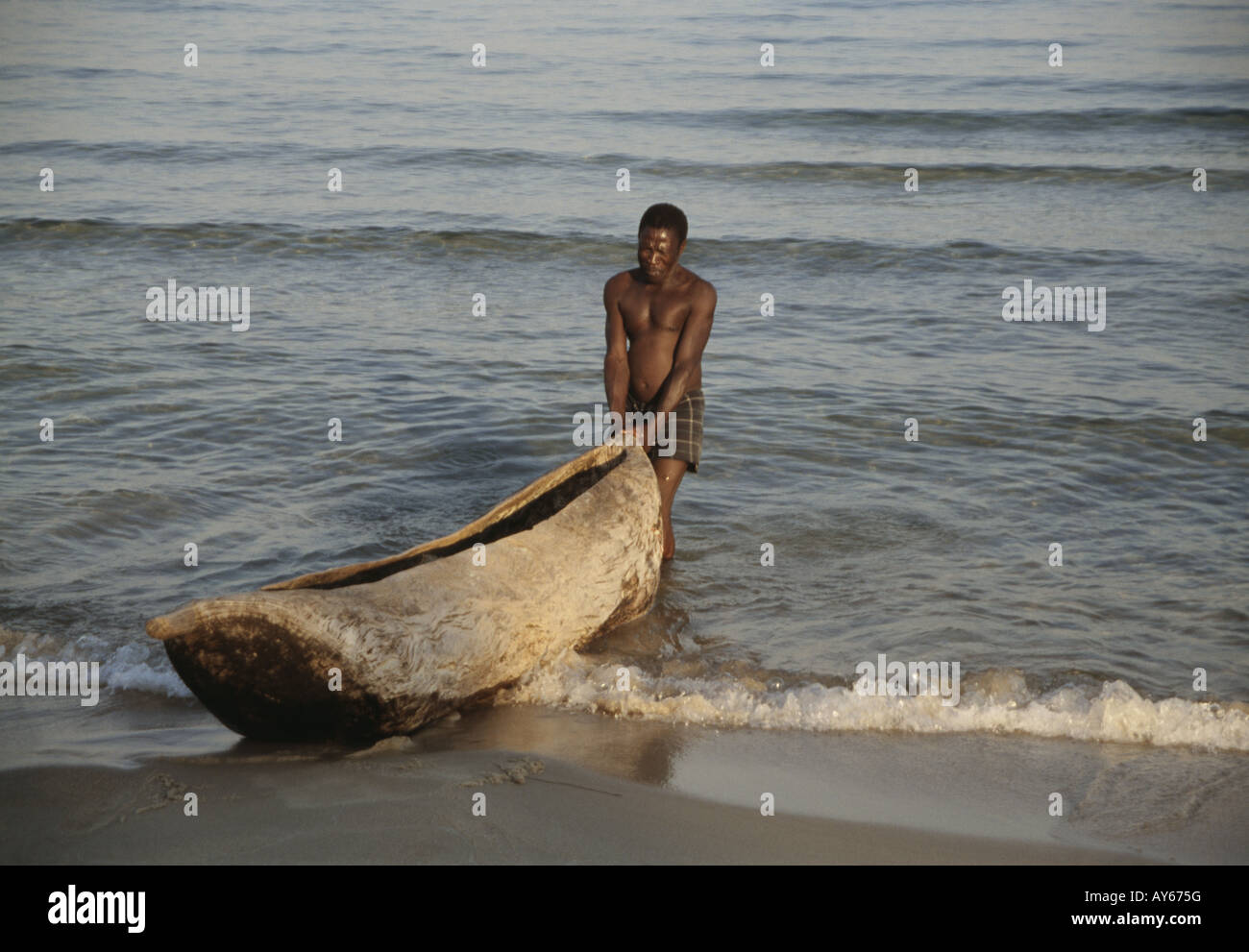 Fisherman pushing small wooden dug out canoe or boat out of the water ...