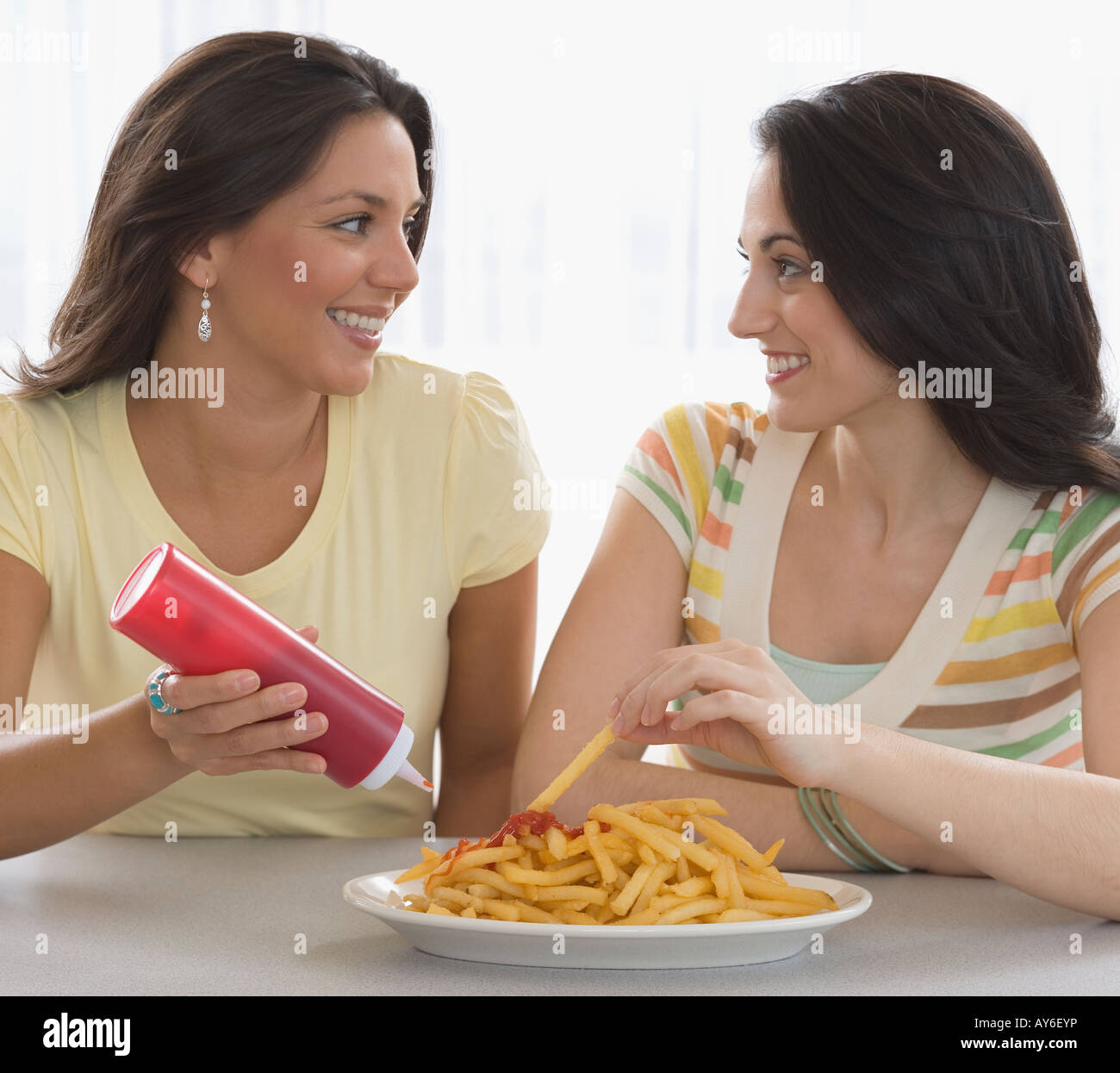 Two young women eating french fries Stock Photo - Alamy