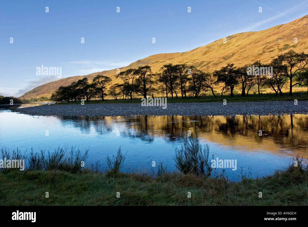 Early Autumn colours with trees silhouetted against bracken on banks of ...