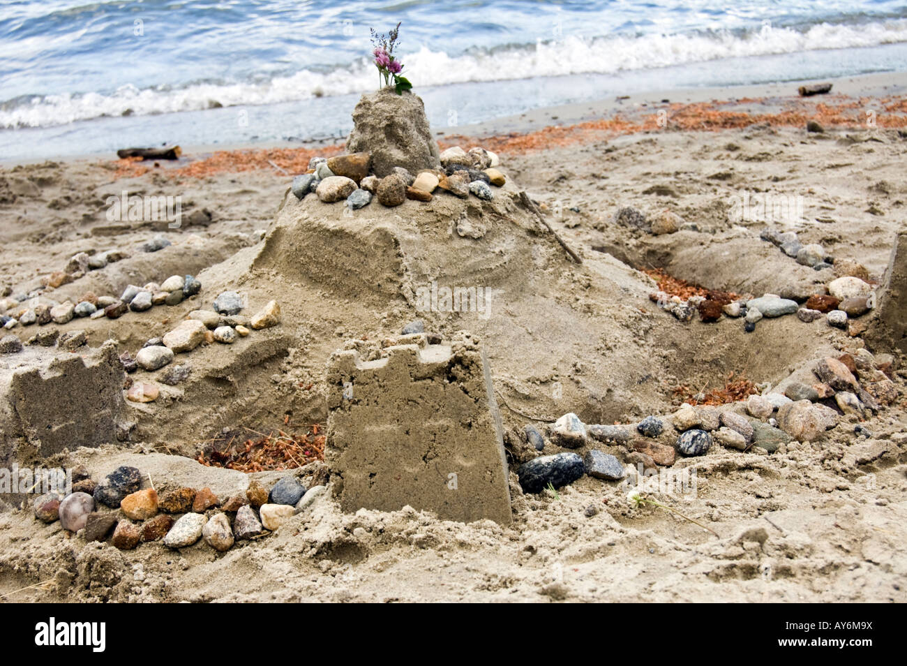 Sandcastle decorated with pebbles and wildflowers at the water s edge ...