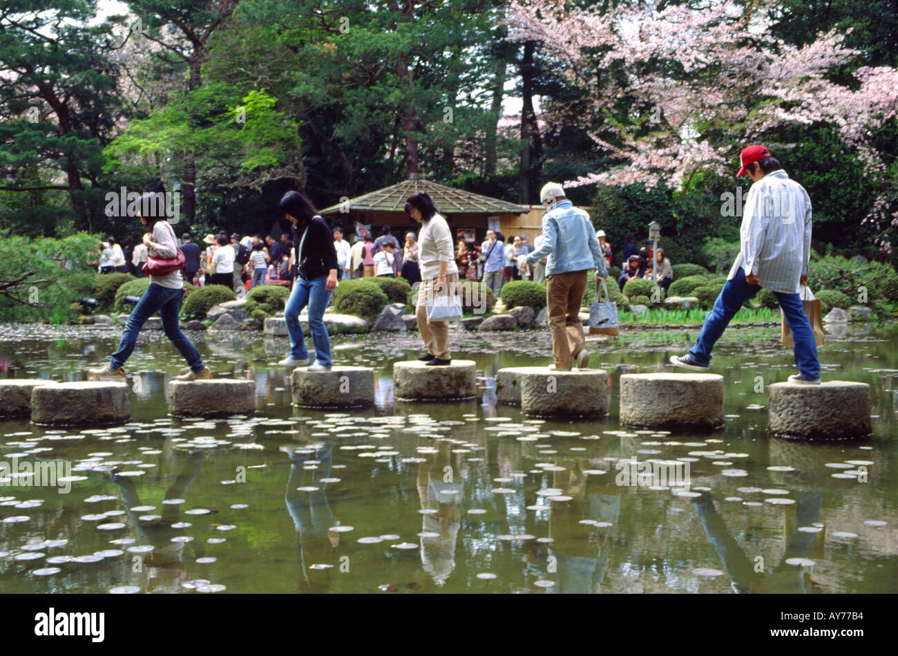 Young Japanese people walking across stepping stones over pond at Heian ...