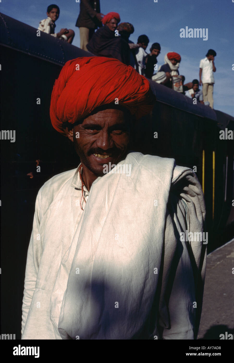 INDIA Portrait of a man standing in front of a train with passengers on ...