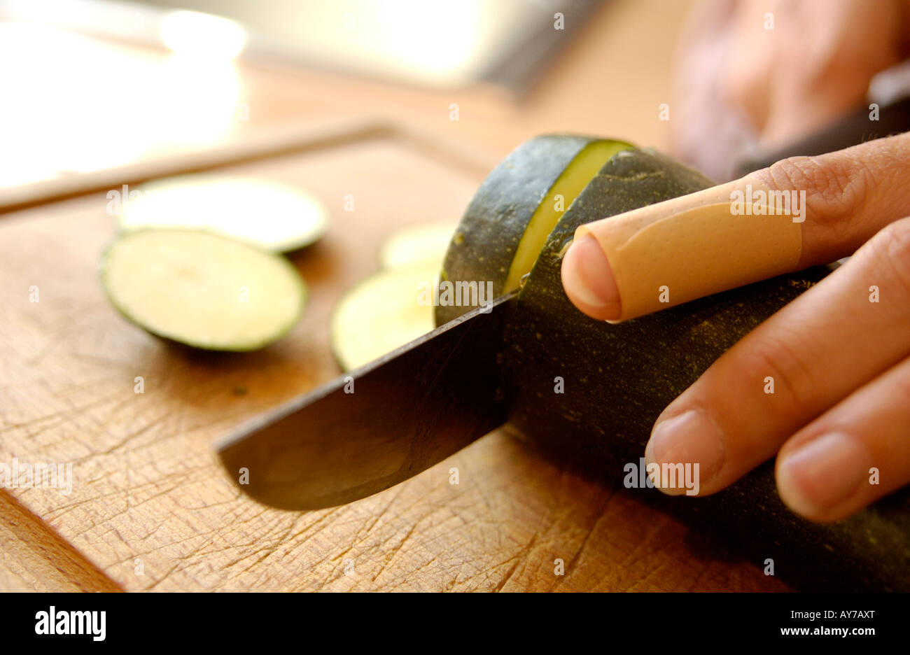 Woman chopping zucchinis / courgettes with a plaster on her finger ...