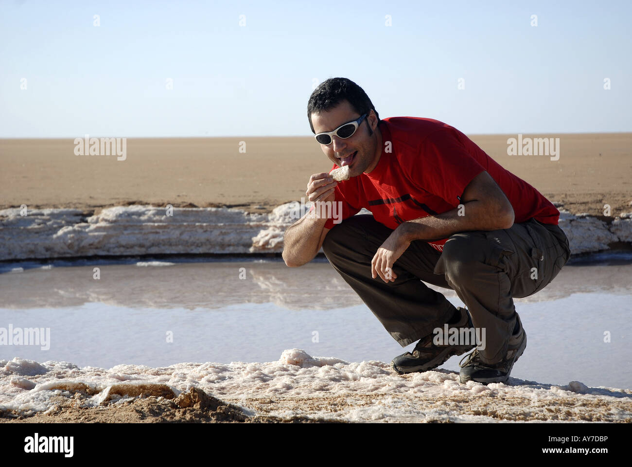 Young man eating salt on flat salt Chott el Jerid salted lake Tunisia ...