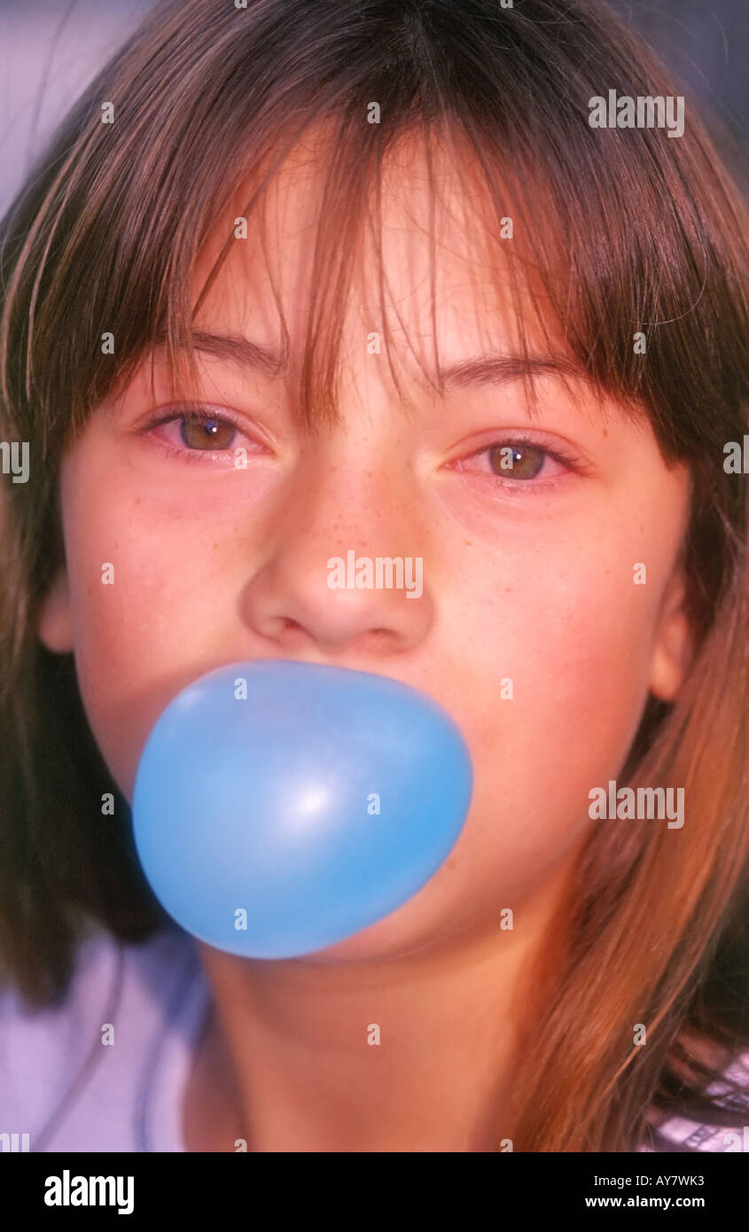 A portrait of a young teenager chewing bubble gum and blowing a blue ...