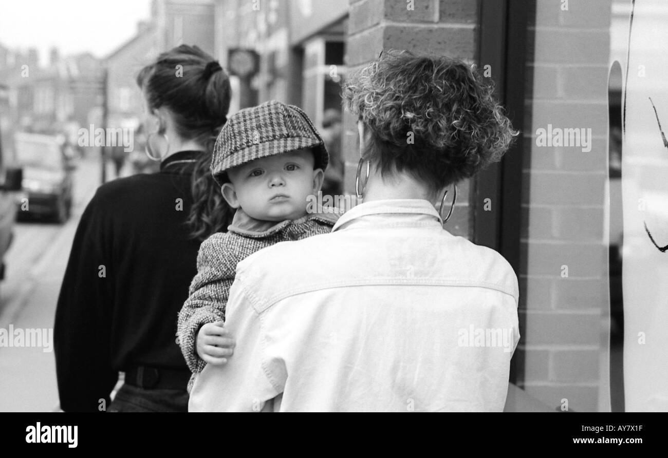 Very young child looking over father’s shoulder wearing a tweed hat ...