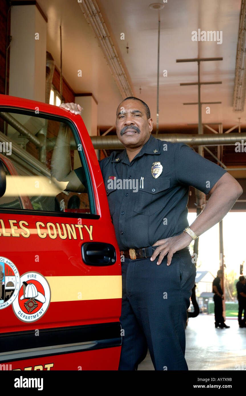 Portrait of African-American male firefighter standing beside firetruck ...