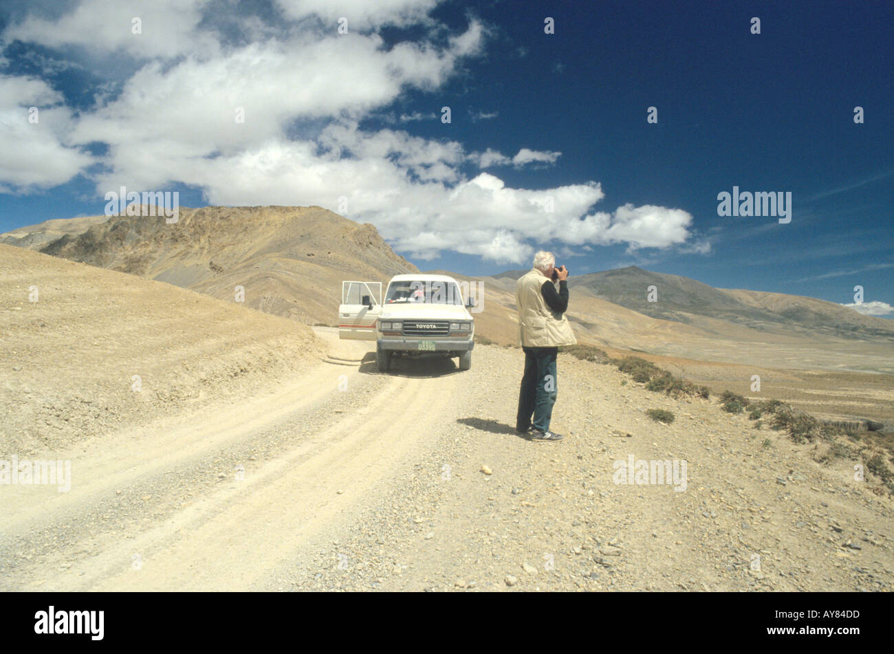 Lone tourist photographing and Toyota Jeep on the long sandy road to ...