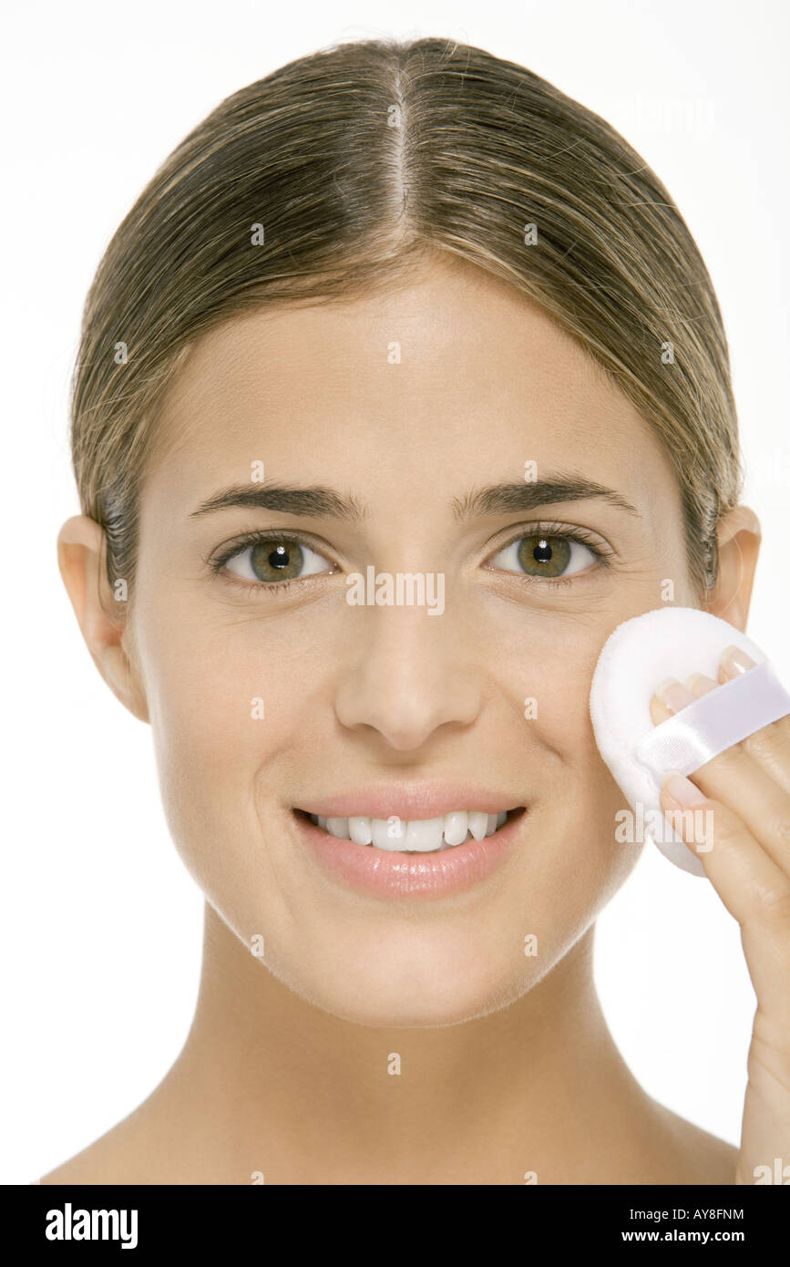 Woman using powder puff on cheek, smiling at camera, close-up Stock ...