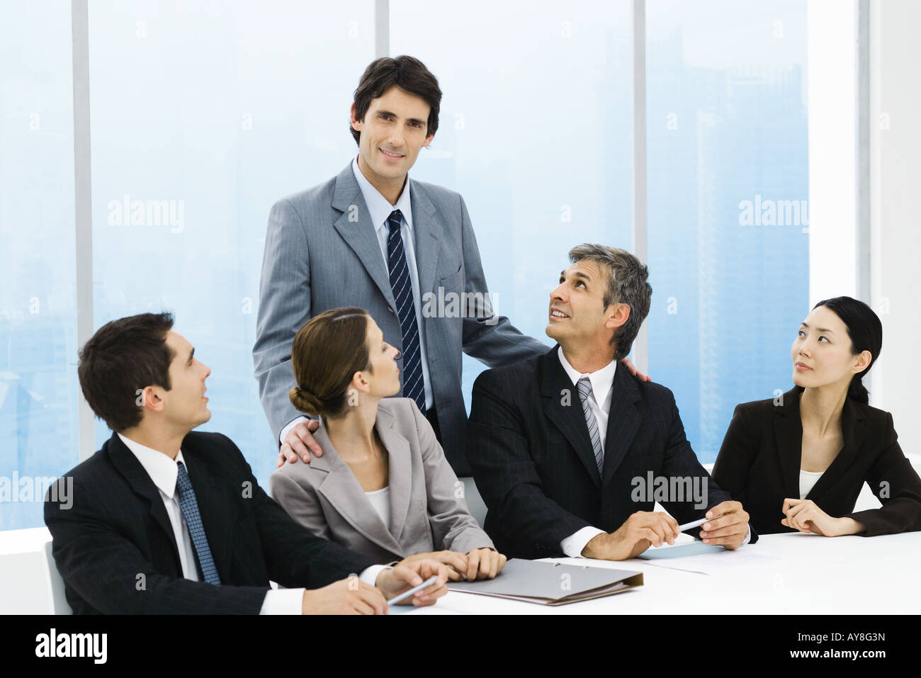 Business leader standing behind group of colleagues at meeting table ...