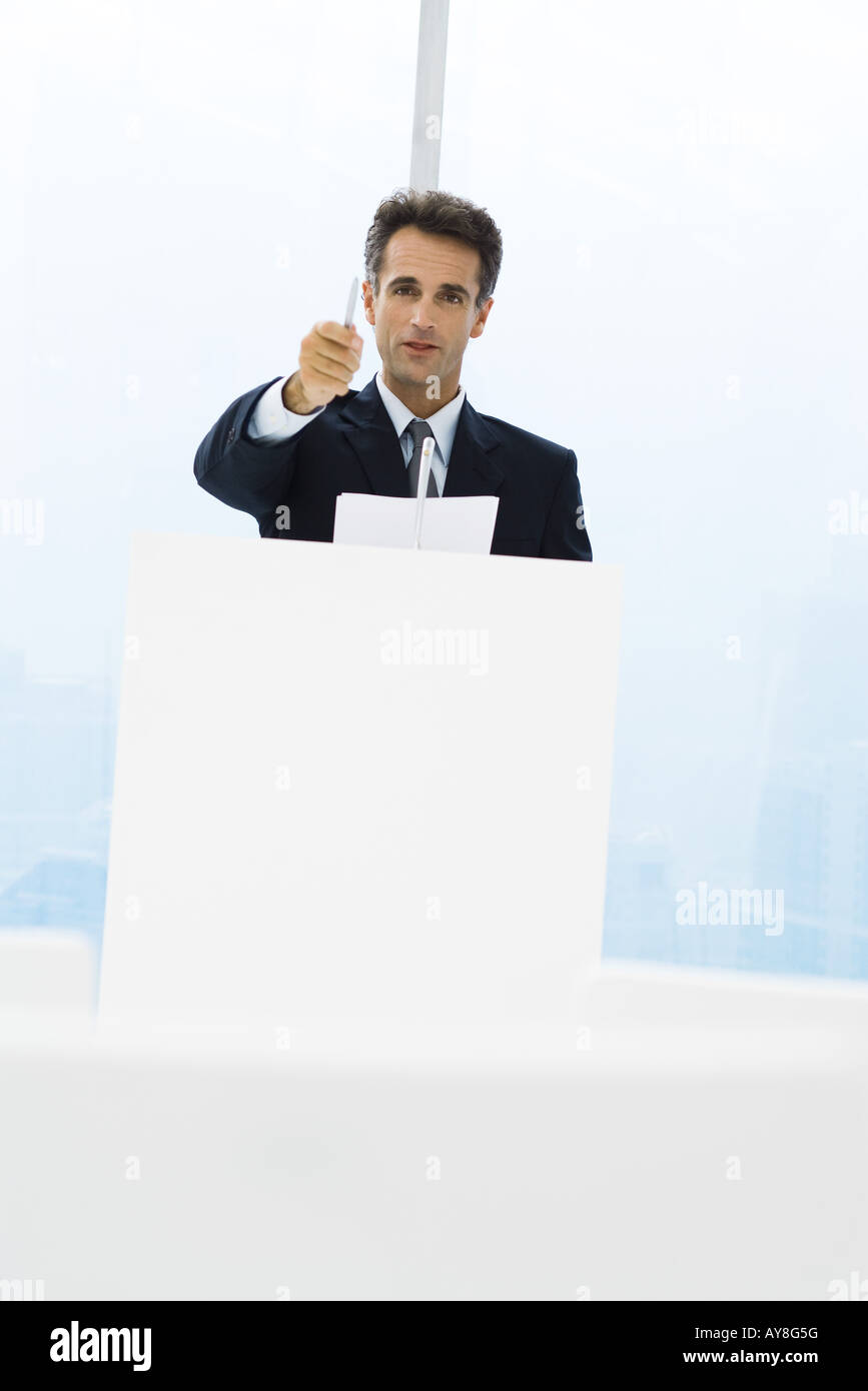 Executive standing behind lectern, pointing with pen at camera Stock ...