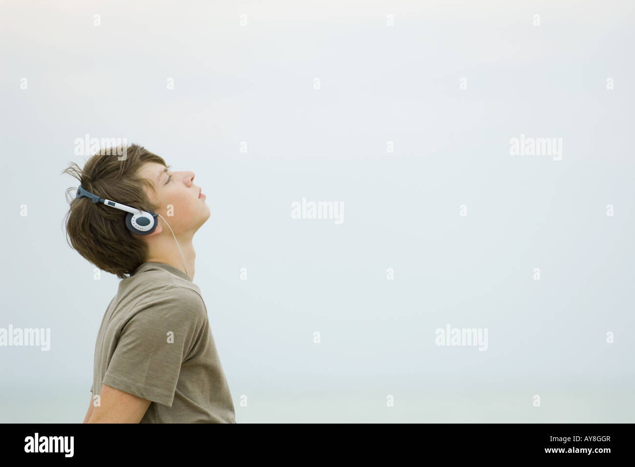 Teenage boy listening to headphones, looking up, side view Stock Photo ...