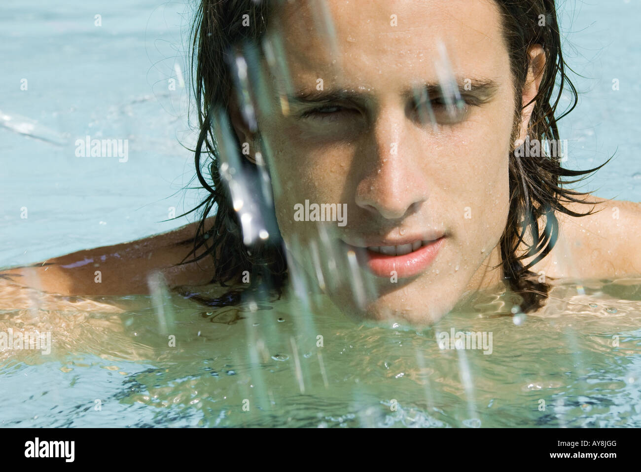 Man in swimming pool, looking at camera through splashing water, close ...