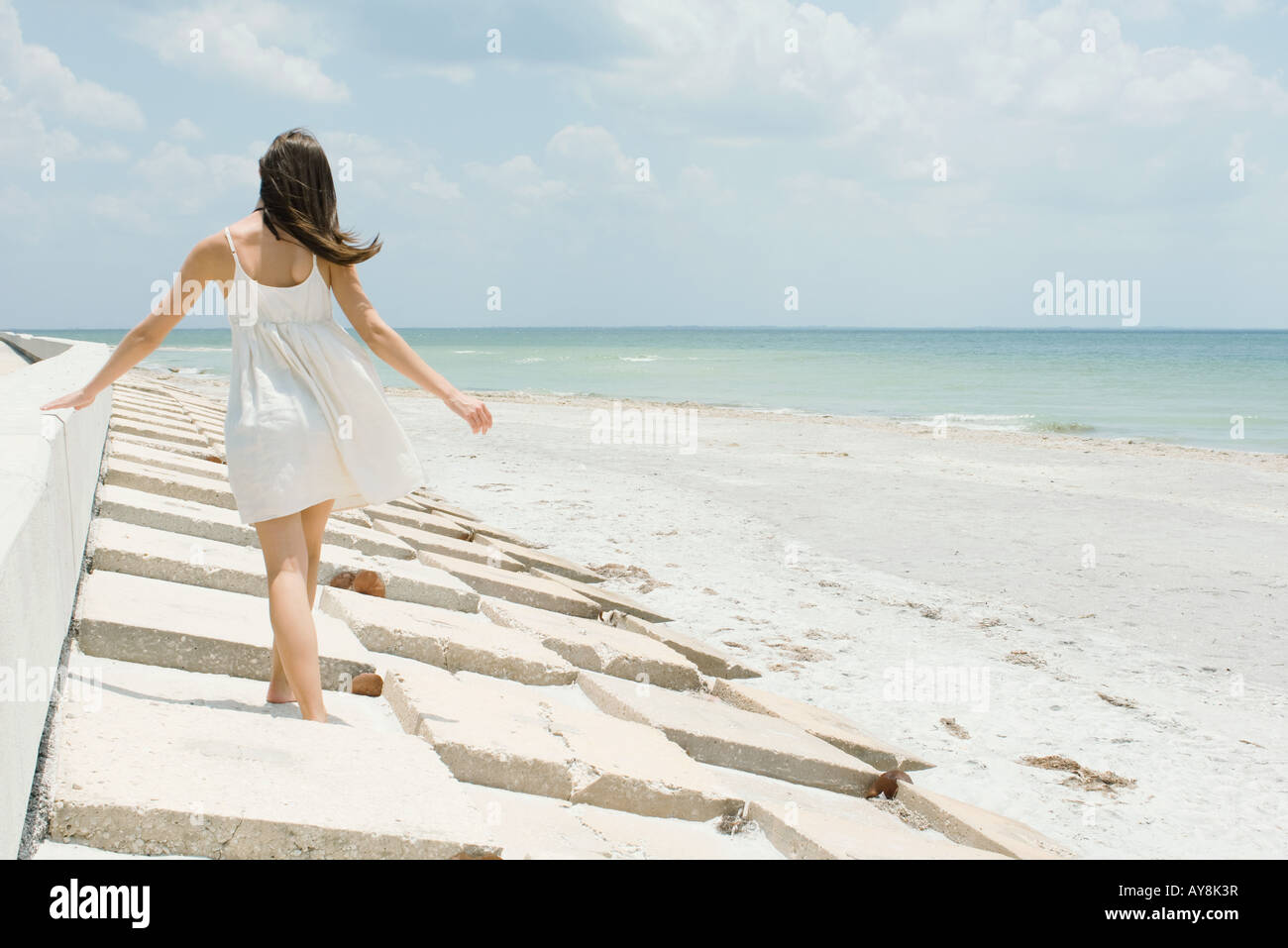 Young woman walking along low wall at the beach, rear view Stock Photo ...