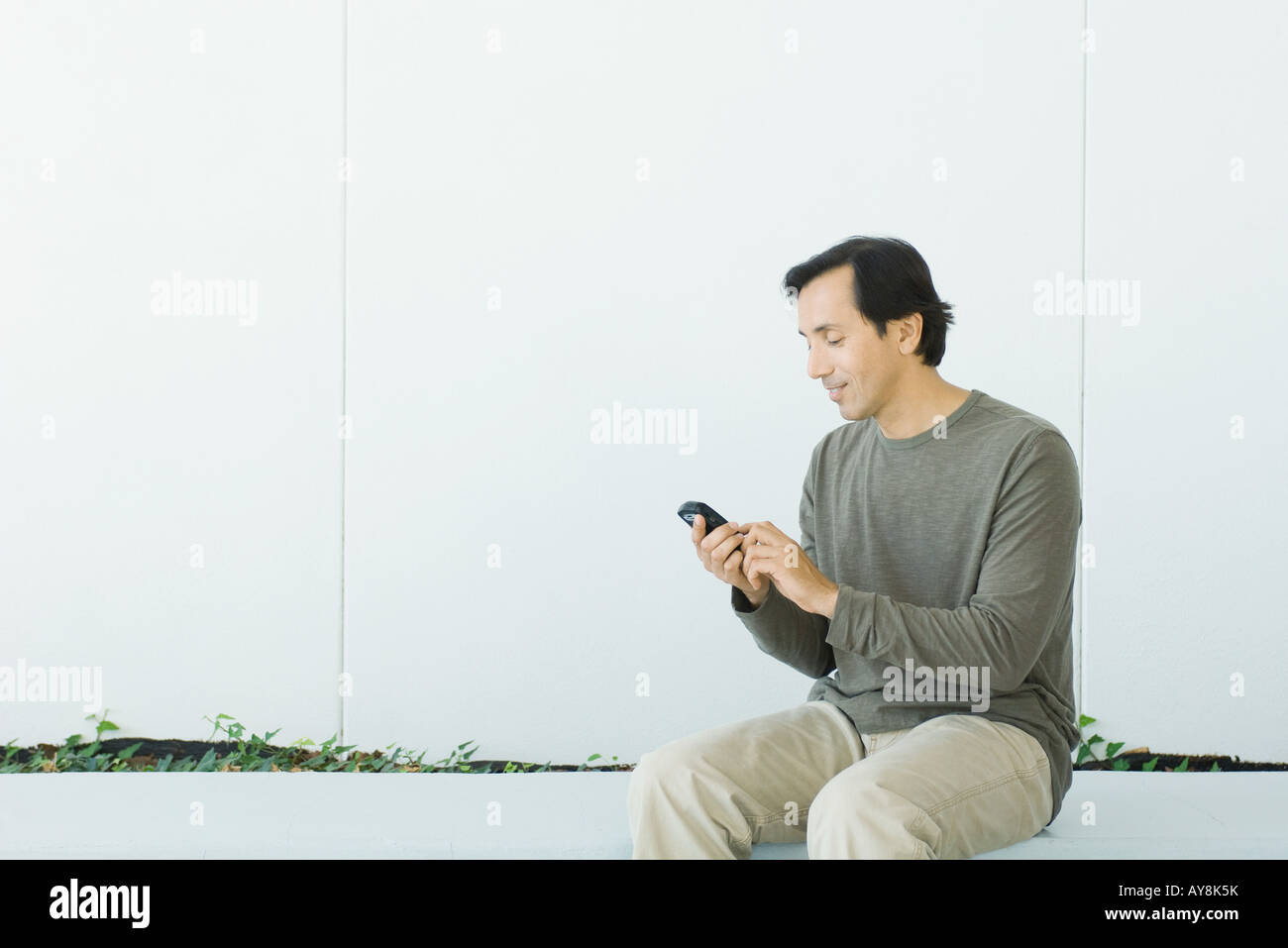 Man sitting, looking down at cell phone, smiling Stock Photo - Alamy
