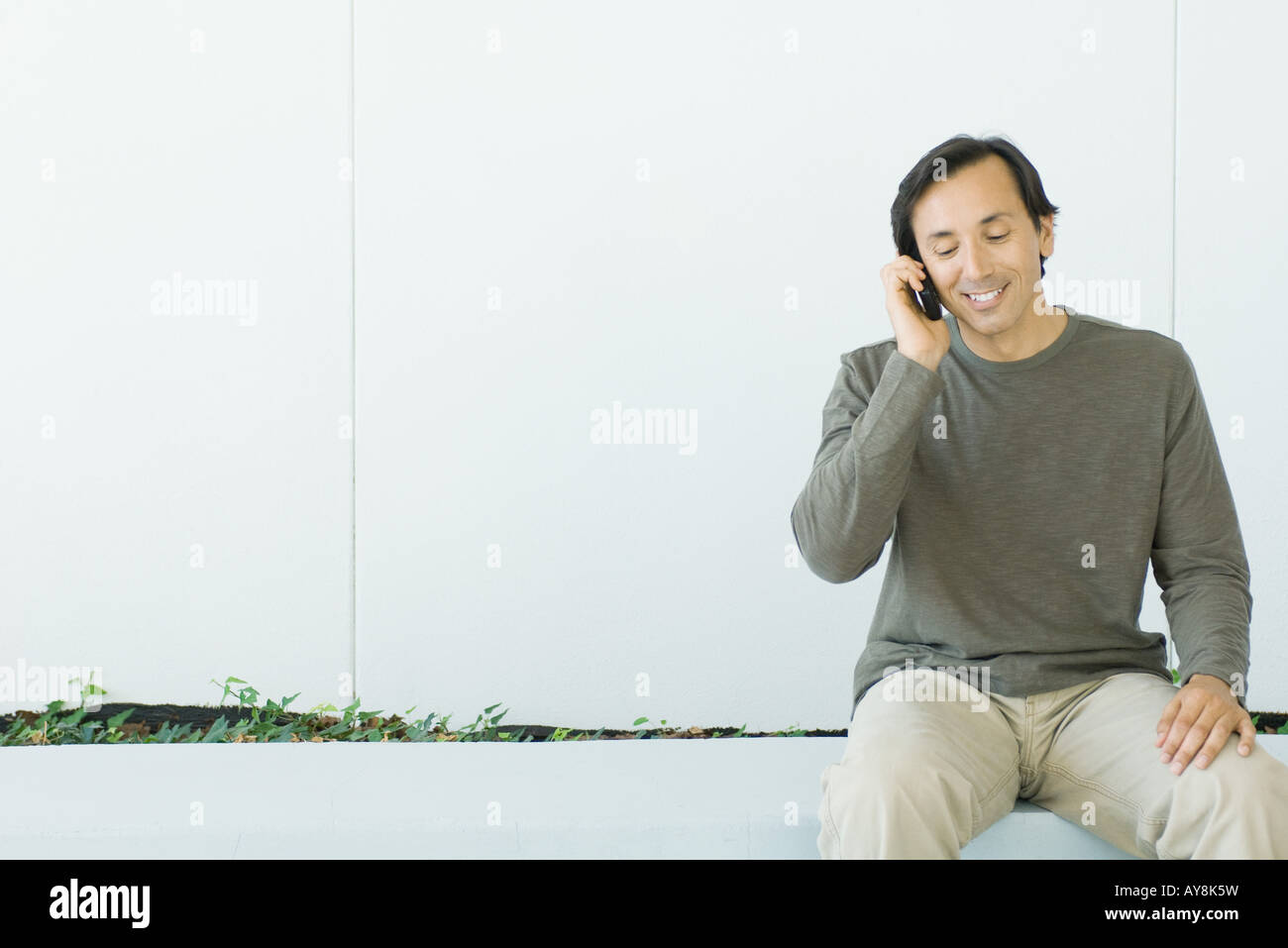 Man sitting, using cell phone, smiling, looking down Stock Photo - Alamy
