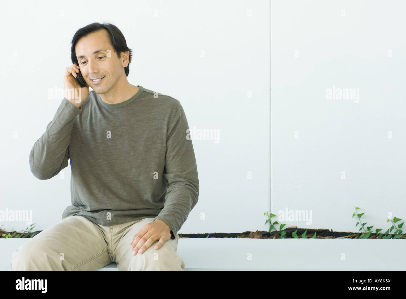 Man sitting, using cell phone, smiling, looking down Stock Photo - Alamy