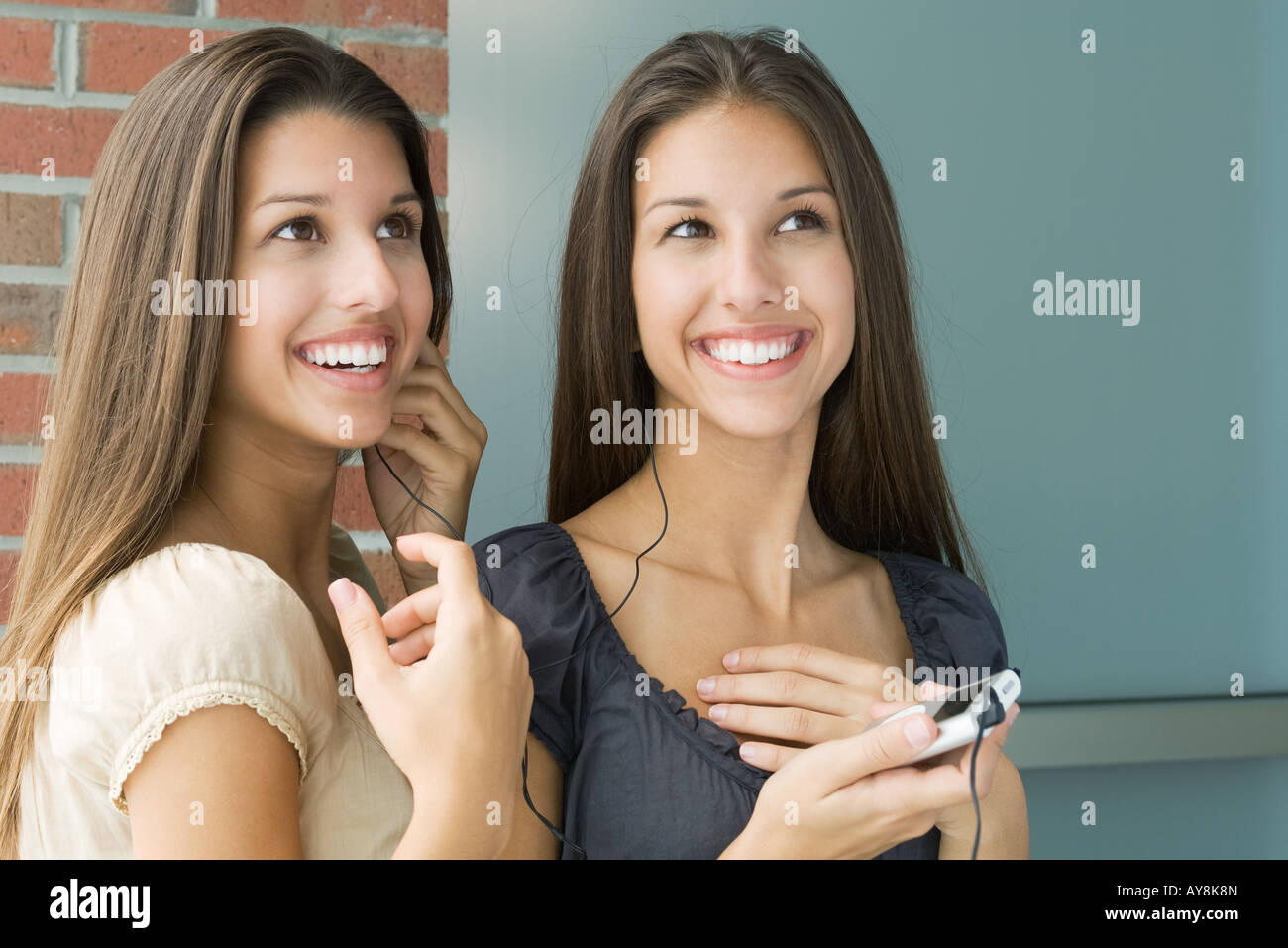 Teenage twin sisters listening to mp3 player together, both smiling and ...
