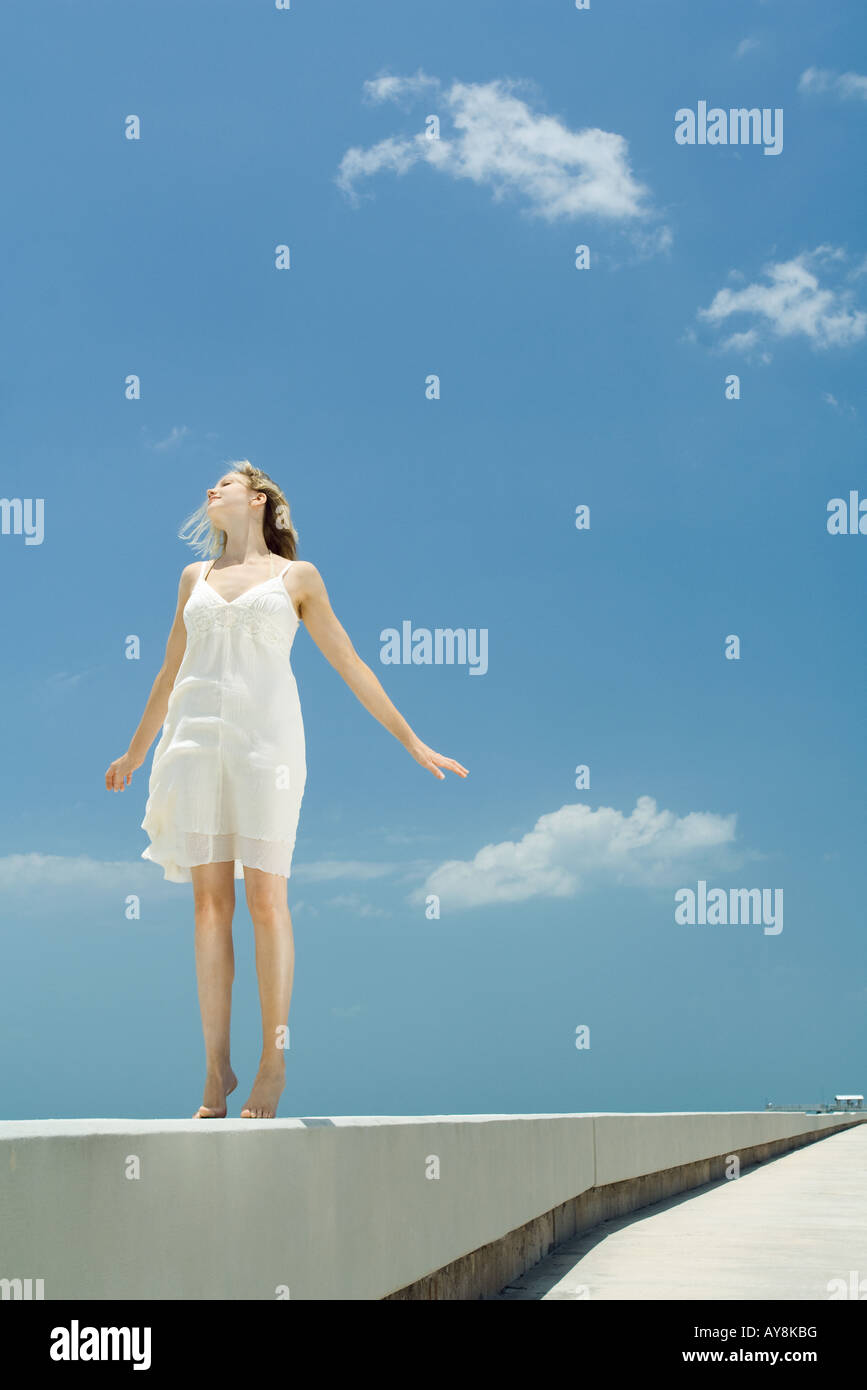 Young woman standing on tiptoe on low wall, arms out, head back Stock ...