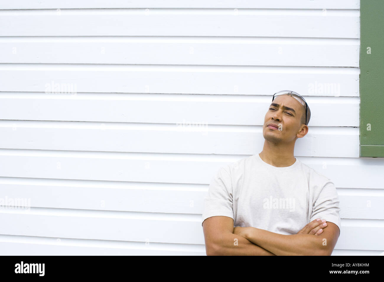 Man leaning against side of house, arms folded, looking up Stock Photo ...