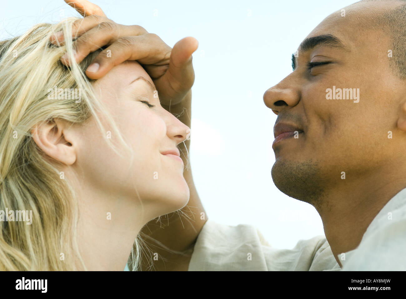 Man placing hand on woman's forehead, both with eyes closed, side view ...