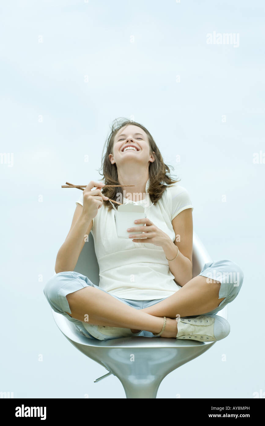 Teenage girl sitting in chair, holding chopsticks and take out food ...
