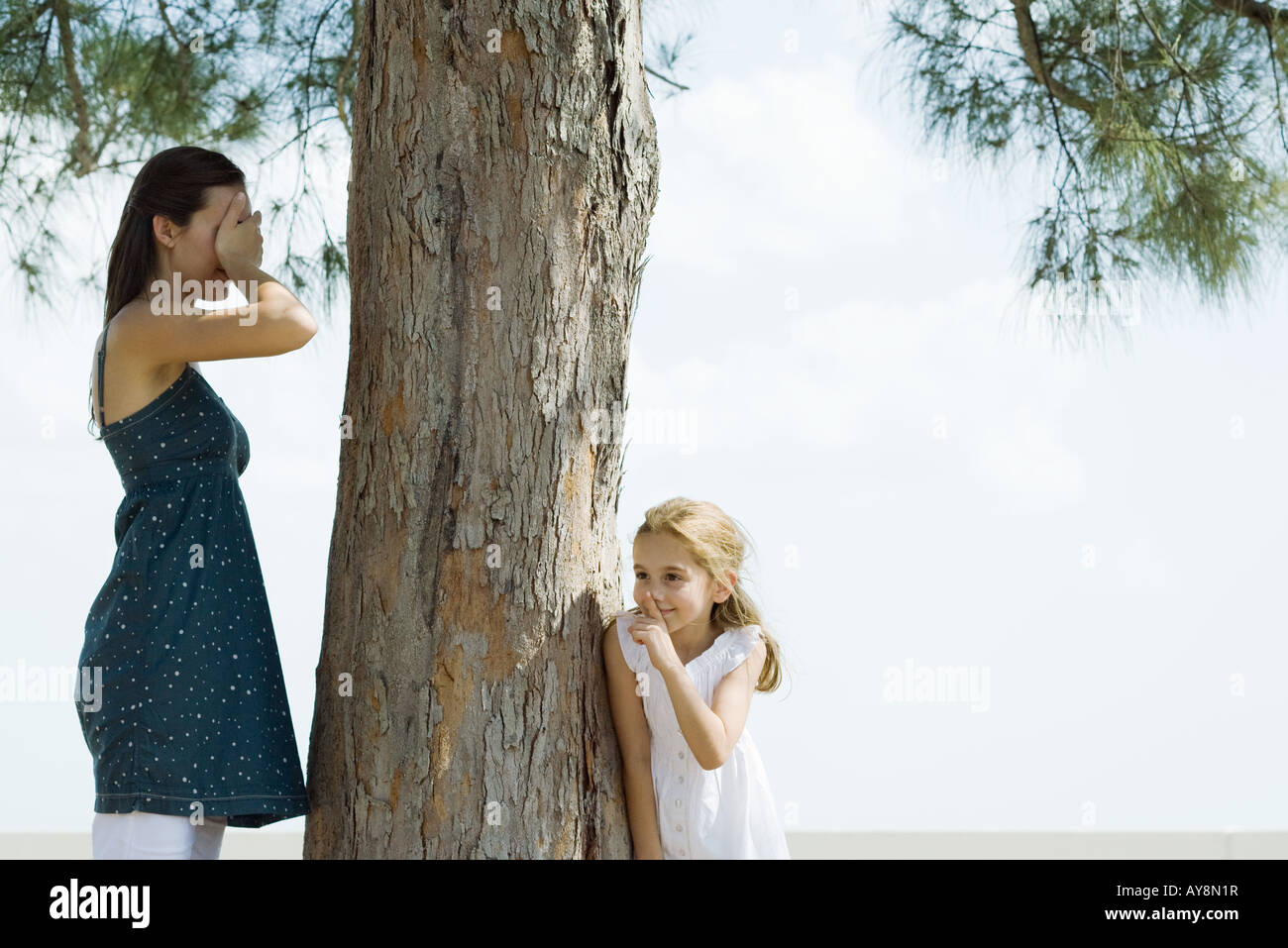 Two sisters playing hide-and-seek, one covering eyes with hands, the ...