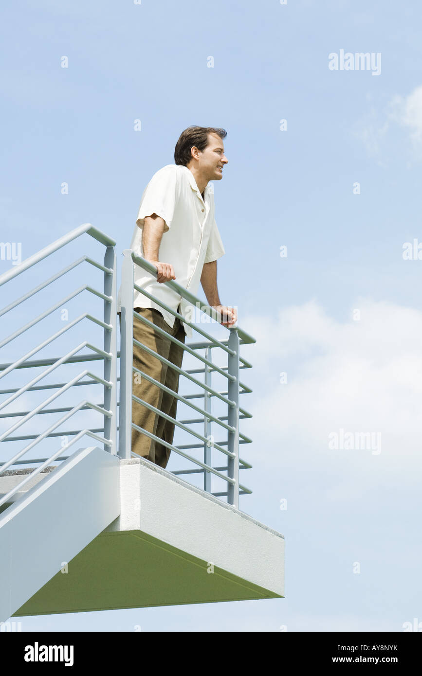 Man leaning against railing, looking into distance, low angle view ...