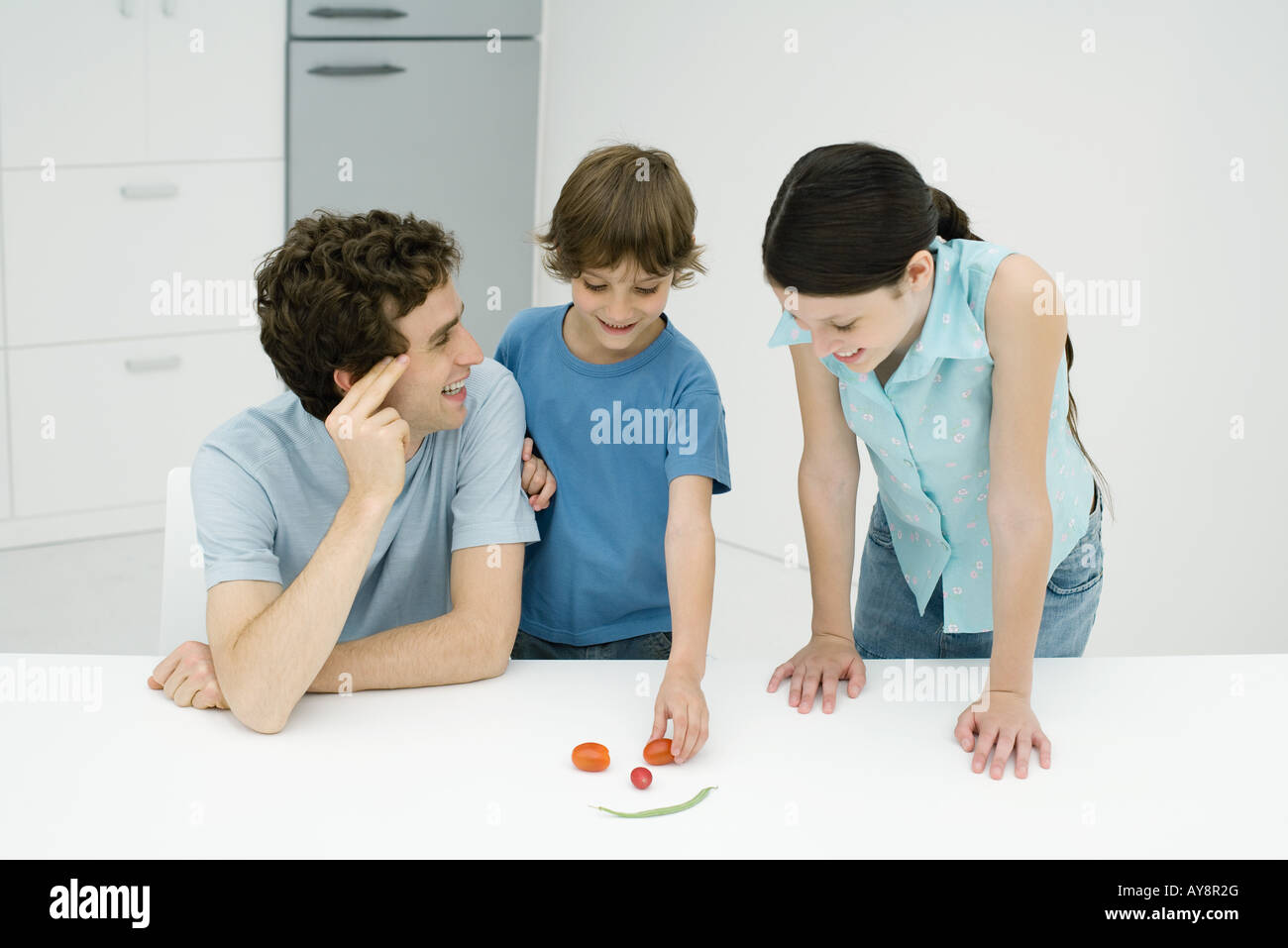 Father and two children in kitchen, making smiley face out of ...