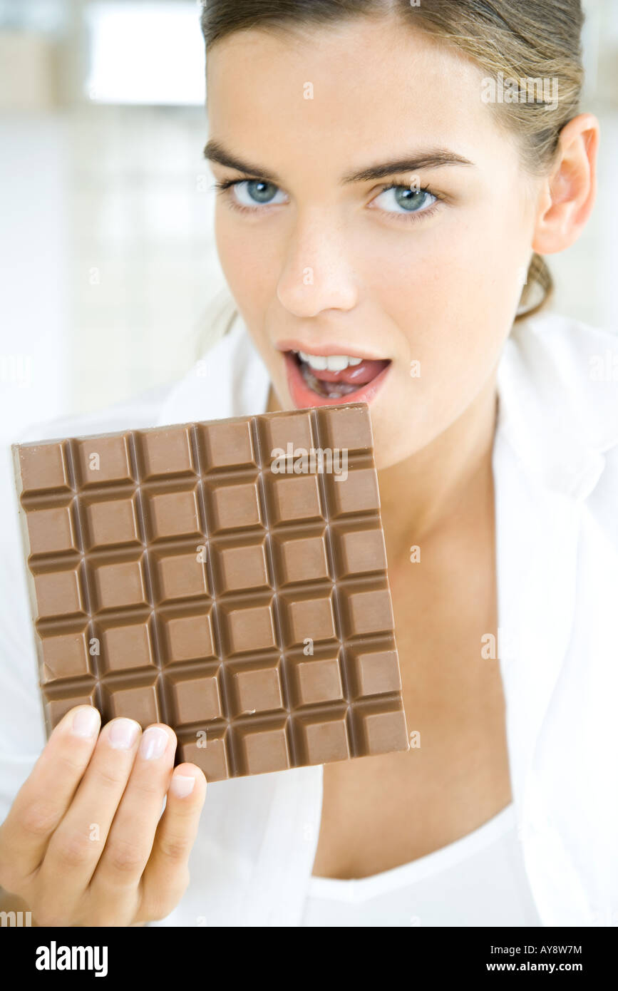 Woman biting into large chocolate bar, looking at camera Stock Photo ...