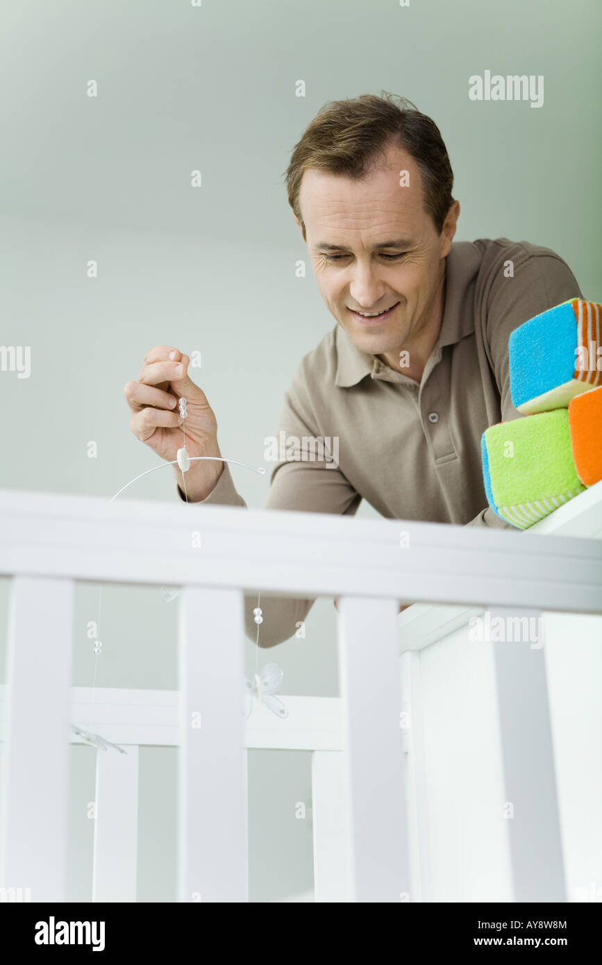 Man leaning over baby crib, holding mobile, looking down Stock Photo ...