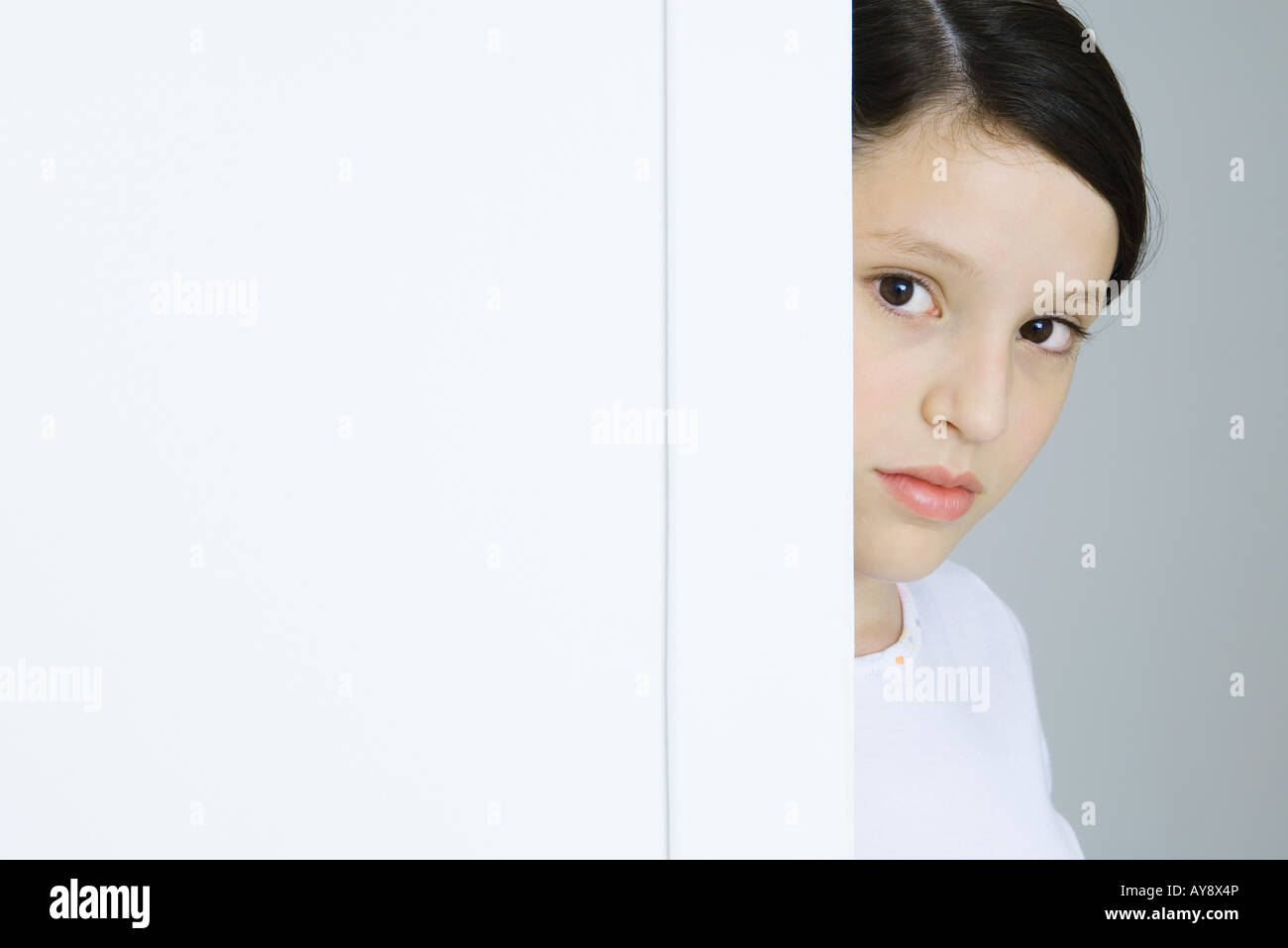 Preteen girl looking around corner of wall, cropped Stock Photo - Alamy