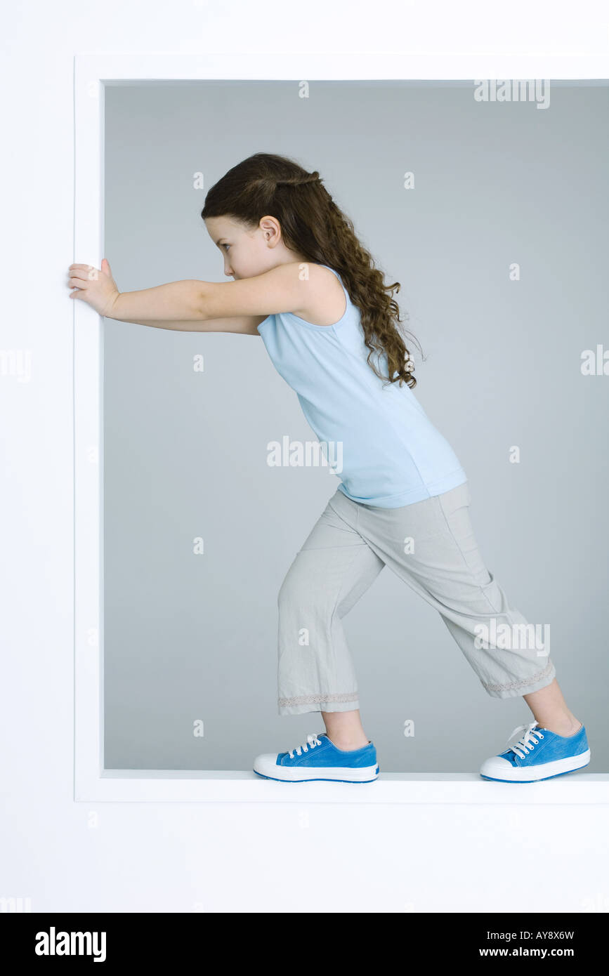 Little girl standing inside window frame, pushing edge, full length ...