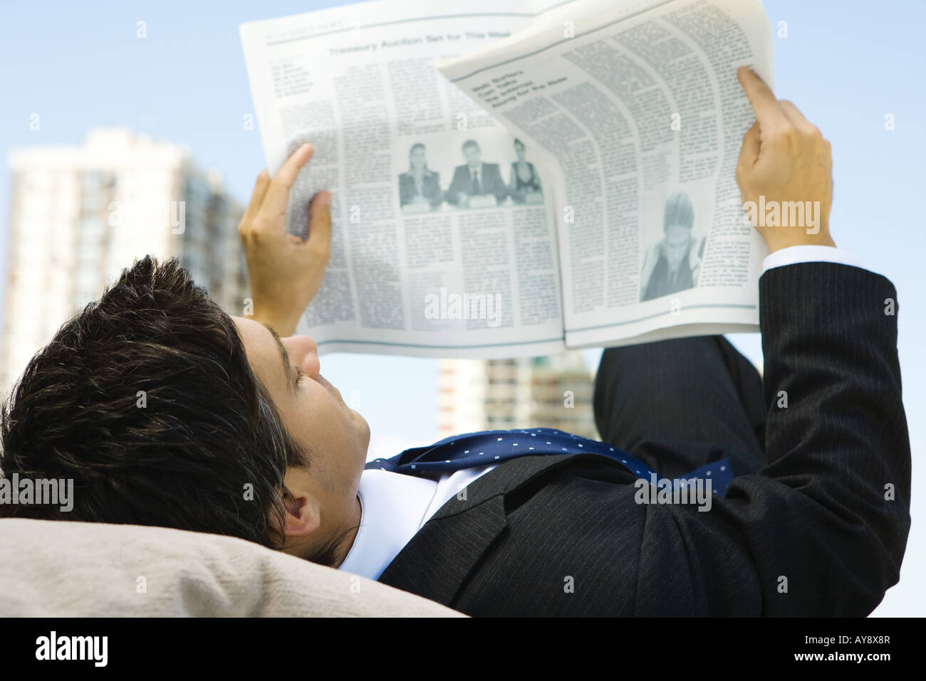 Businessman lounging outdoors, reading newspaper Stock Photo - Alamy