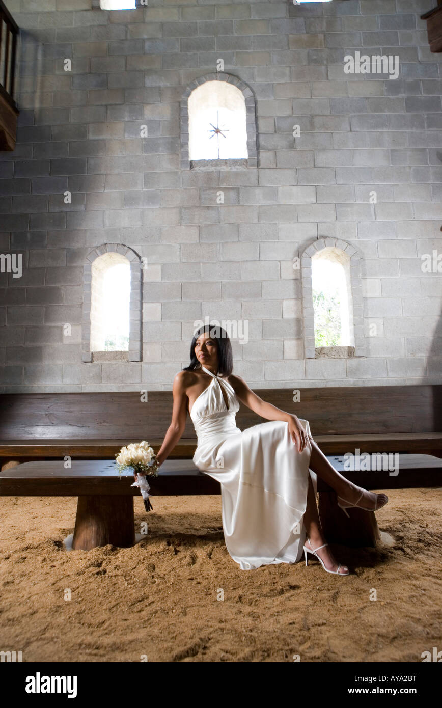 Portrait of a young bride in a white gown sitting on a bench inside a ...