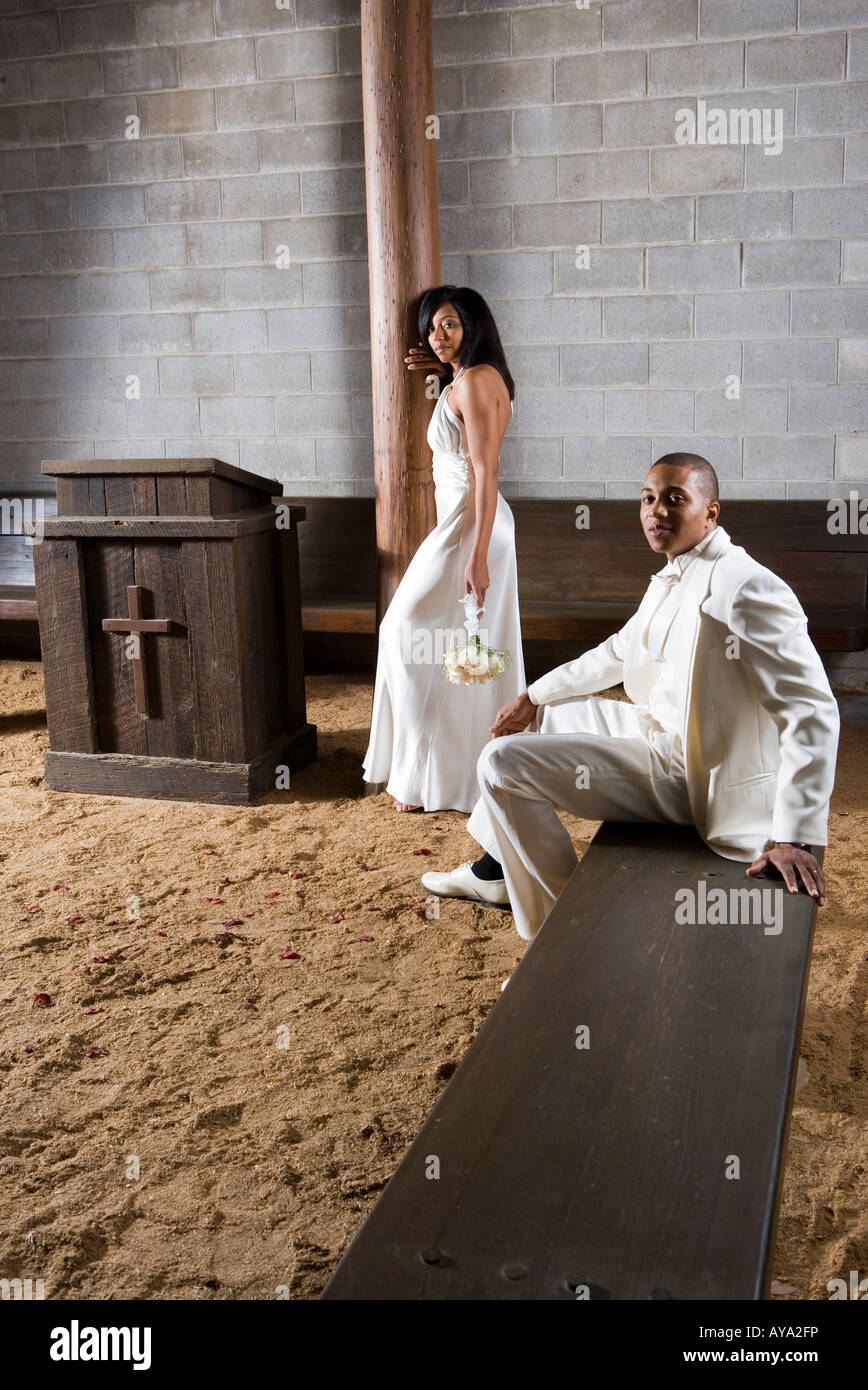 A bride standing next to a groom seated on a bench, all in white Stock ...