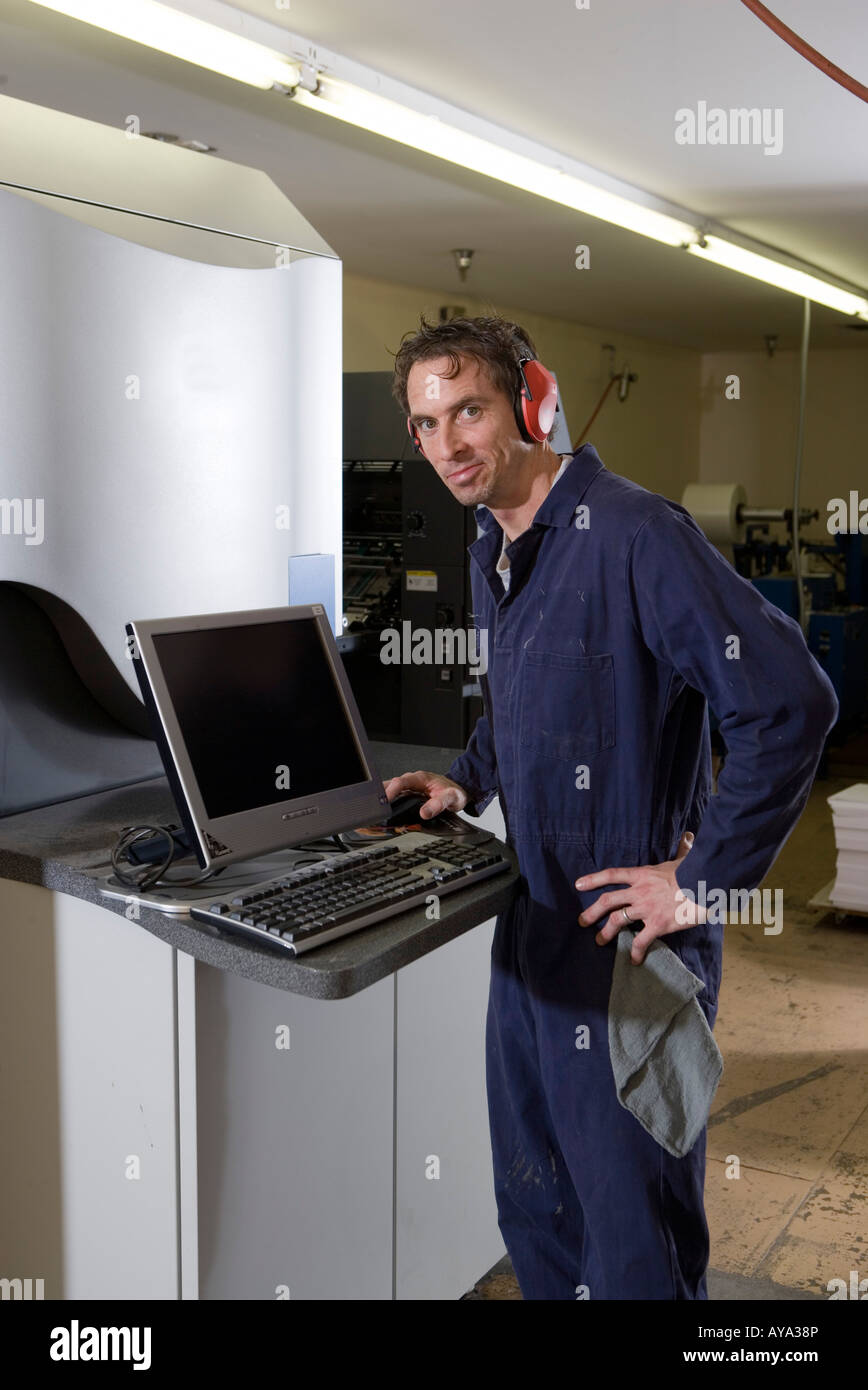 View of a man in coveralls operating a machine by using a computer ...