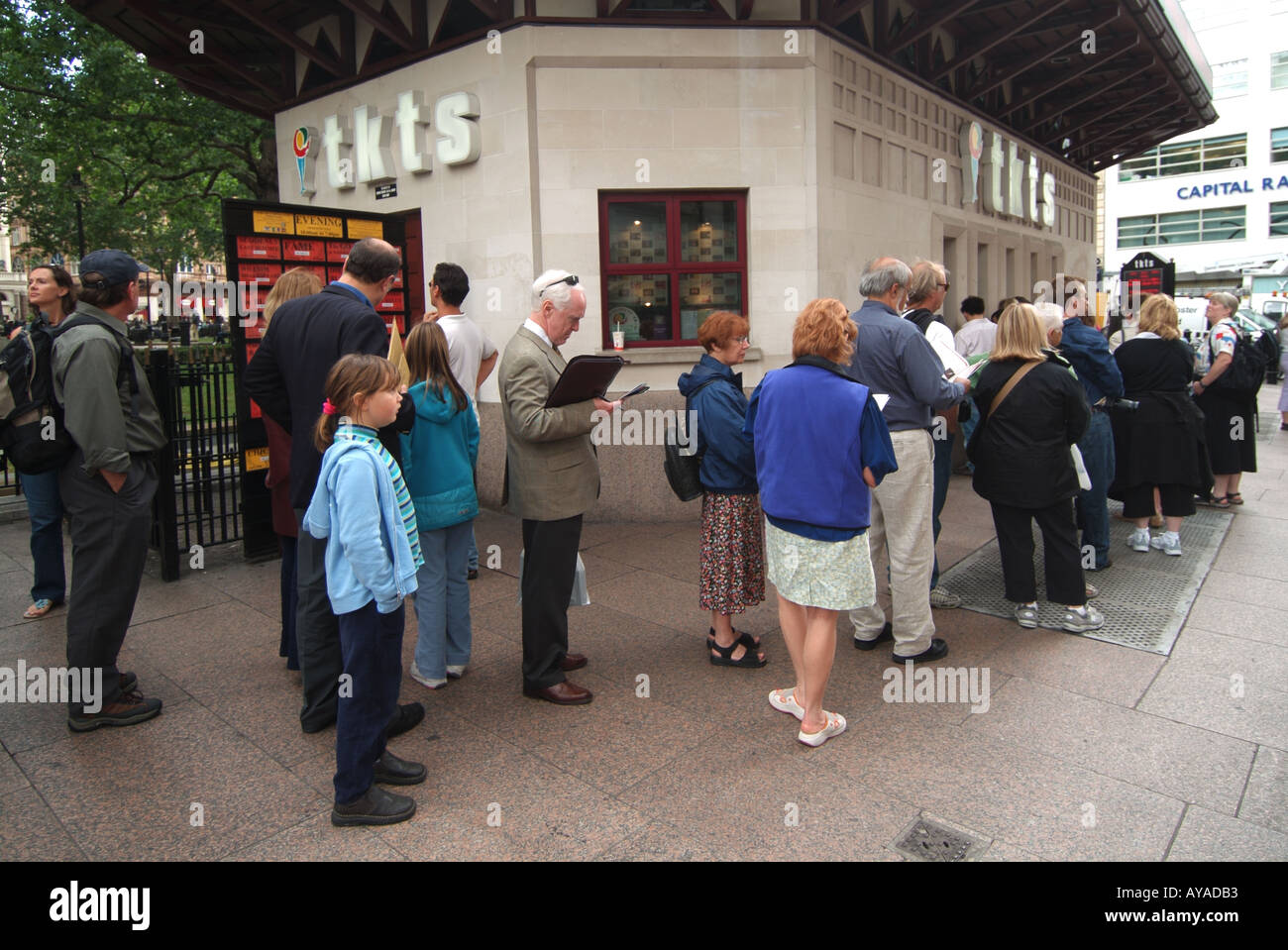 Queue of people waiting to purchase theatre tickets from booking kiosk ...