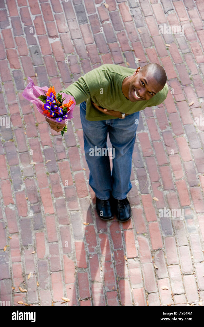 Elevated view of a young man on street, bowing and gesturing upwards ...