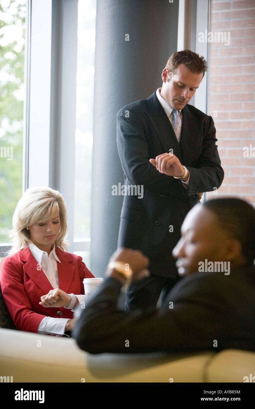 Business people sitting and waiting in an office lobby, looking at ...