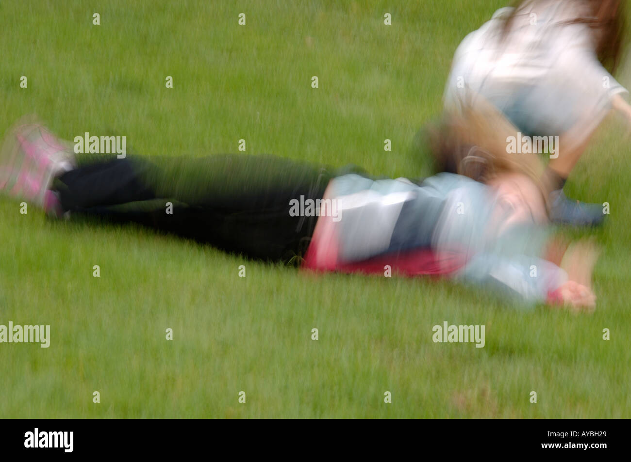 two young girls bodies rolling down hill on the grass Stock Photo - Alamy