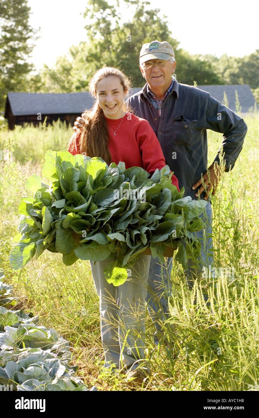 Farmer and his daughter in farm field, holding produce, with barn in ...