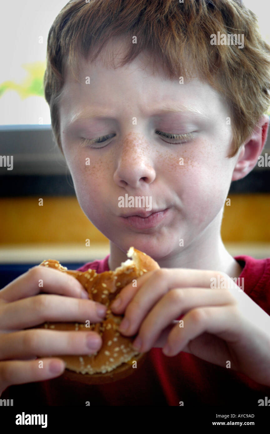 Red haired boy eating a real unhealthy beef hamburger and playing for ...