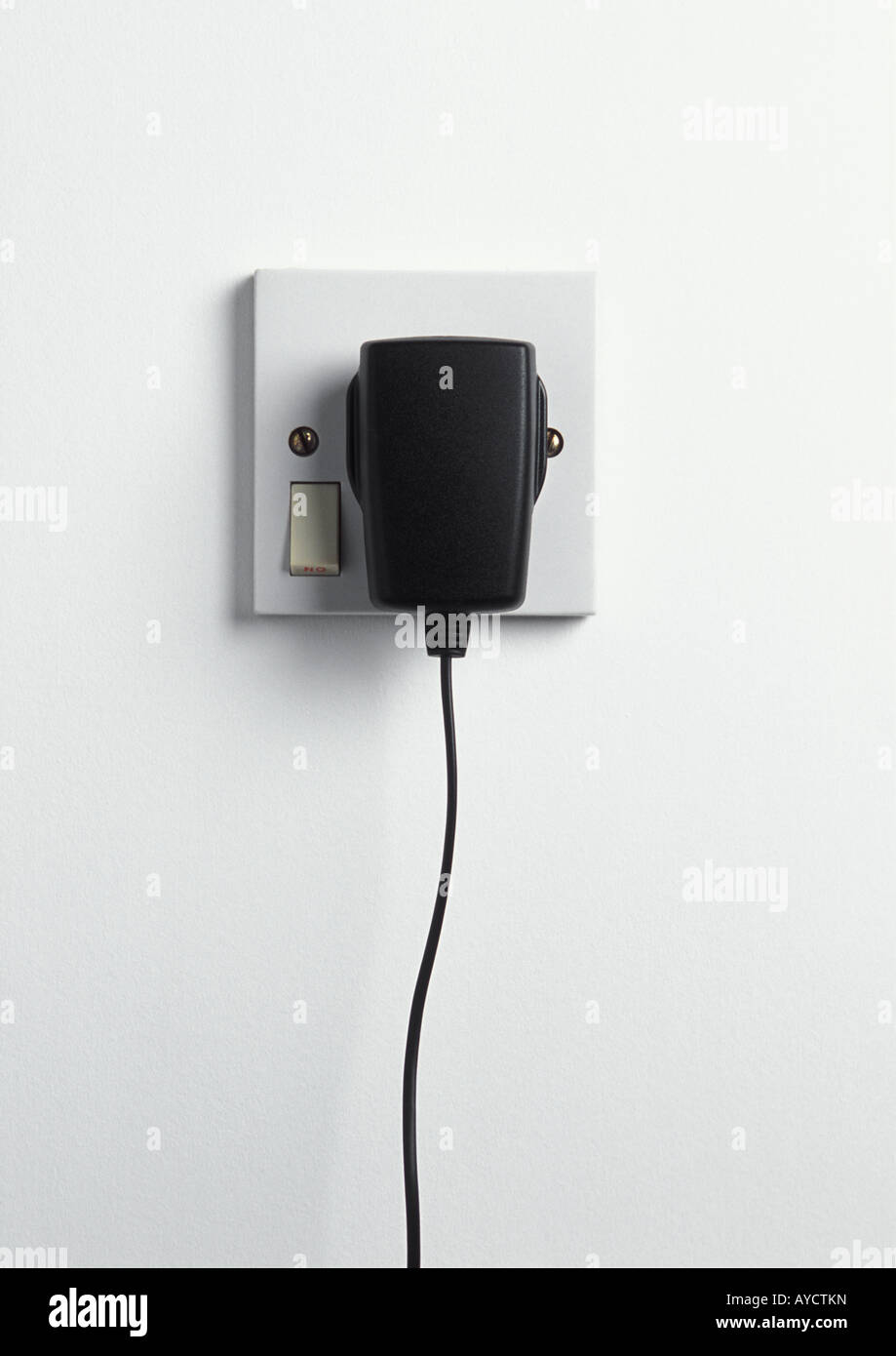 Mobile phone charger plugged into white electrical socket on white wall ...